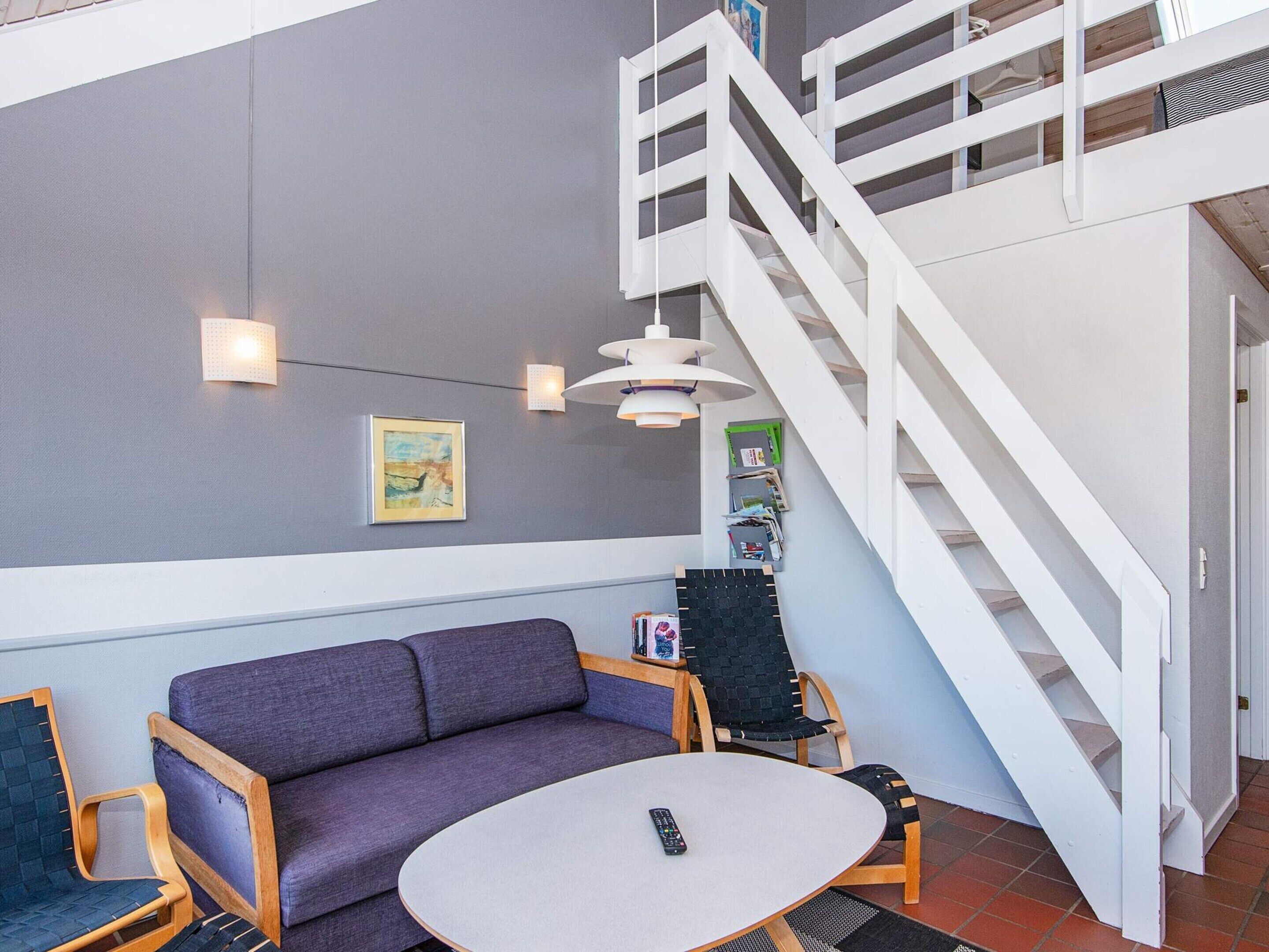 Um interior moderno com sofá, cadeiras, uma mesa, escada e prateleira fixada na parede.