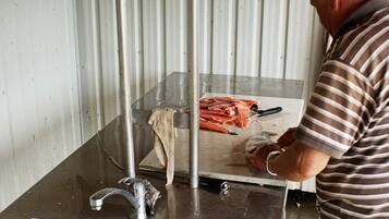 Um homem trabalhando em uma bancada de aço inoxidável, com uma faca e peixe, uma pia e uma toalha pendurada na parede.
