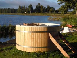 Estrutura de madeira à beira de um lago, possivelmente uma sauna ou banheira de hidromassagem, com uma escada que dá acesso.