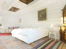 Quarto com uma cama grande, cabeceira de madeira, mesa de cabeceira pequena, abajur e um quadro na parede.