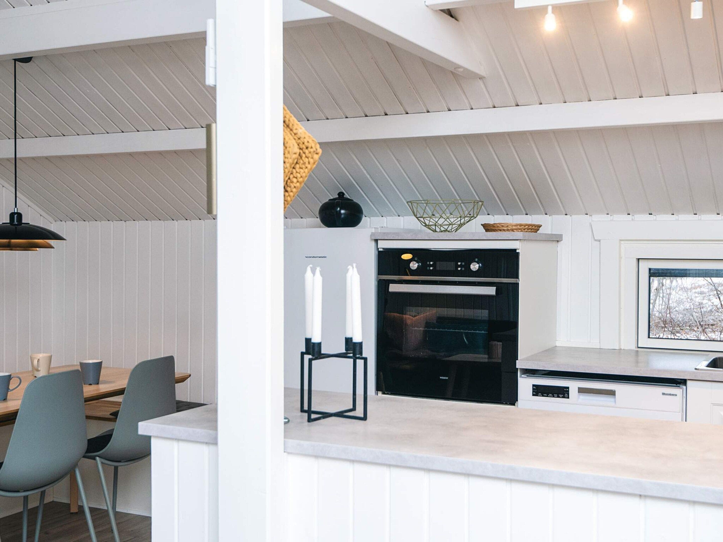 Uma cozinha moderna com forno embutido, área de refeições com cadeiras e uma luminária pendente.