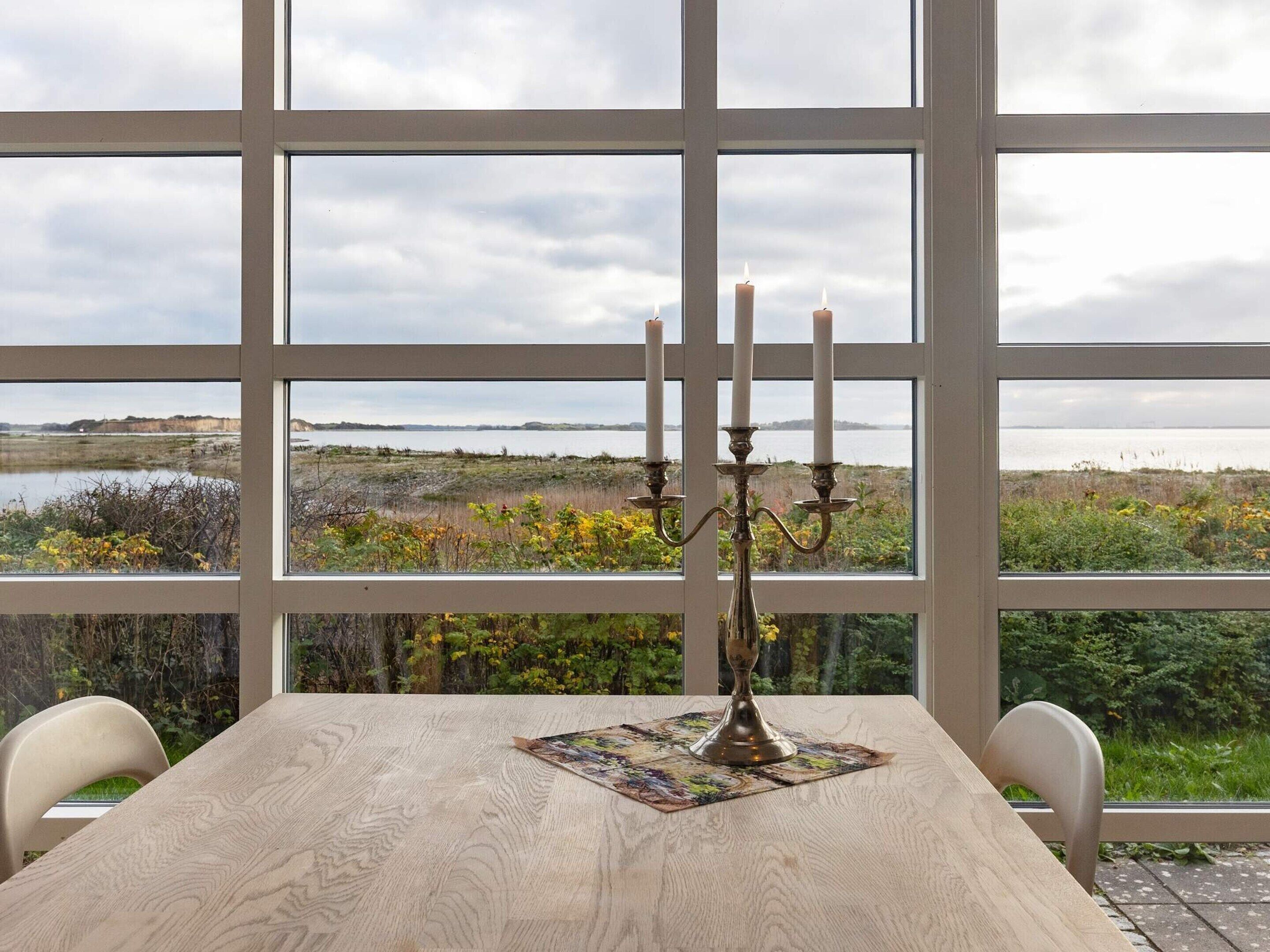 Mesa com castiçal em frente a uma grande janela com vista para uma paisagem natural.