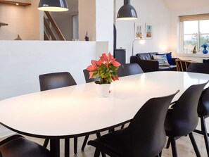 Uma área de refeições moderna com uma mesa branca, cadeiras pretas e um vaso com flores vermelhas.