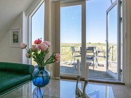 Quarto com mesa de vidro, sofá verde e vista para um deck externo com cadeiras.