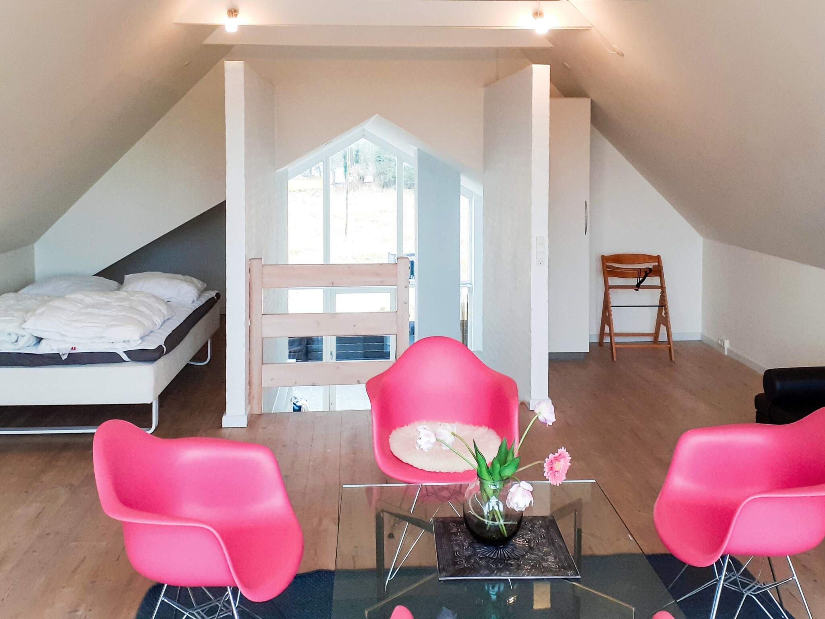 Quarto com cama, uma cadeira de madeira, uma mesa de vidro com um vaso e uma cadeira vermelha.