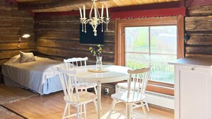 Interior de cabana com cama, mesa de jantar com cadeiras, lustre e janela com vista para vacas.