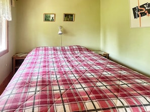 Quarto com uma cama, mesa de cabeceira, abajur e duas fotos emolduradas na parede.