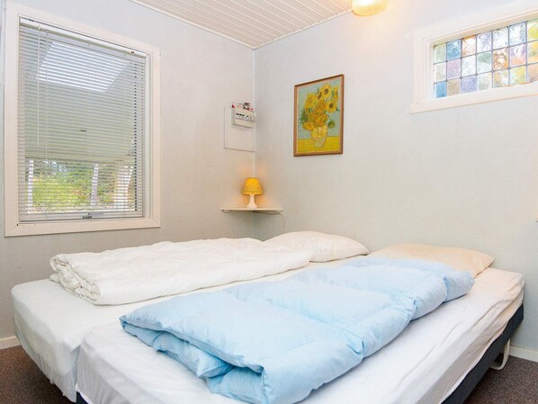 Quarto com duas camas, janela com persianas, luminária na parede e um quadro.