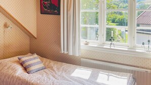 Uma cama de solteiro com colcha estampada, uma janela com cortinas e um radiador embaixo.