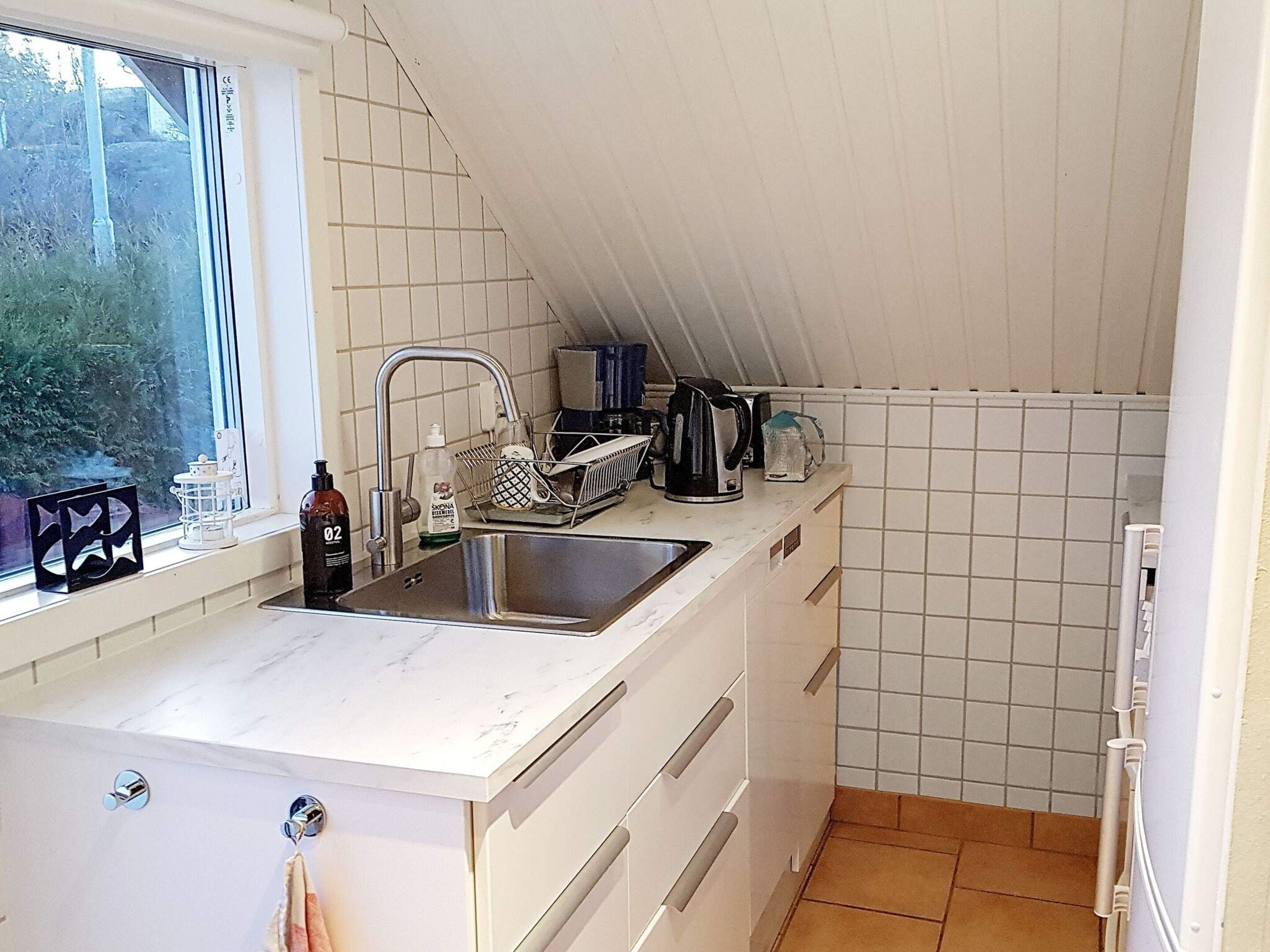 Cozinha compacta com pia, chaleira e janela com vista para vegetação.