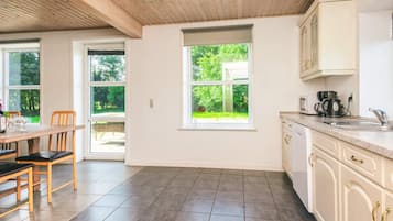 Uma cozinha moderna com armários brancos, piso ladrilhado e grandes janelas com vista para o verde.