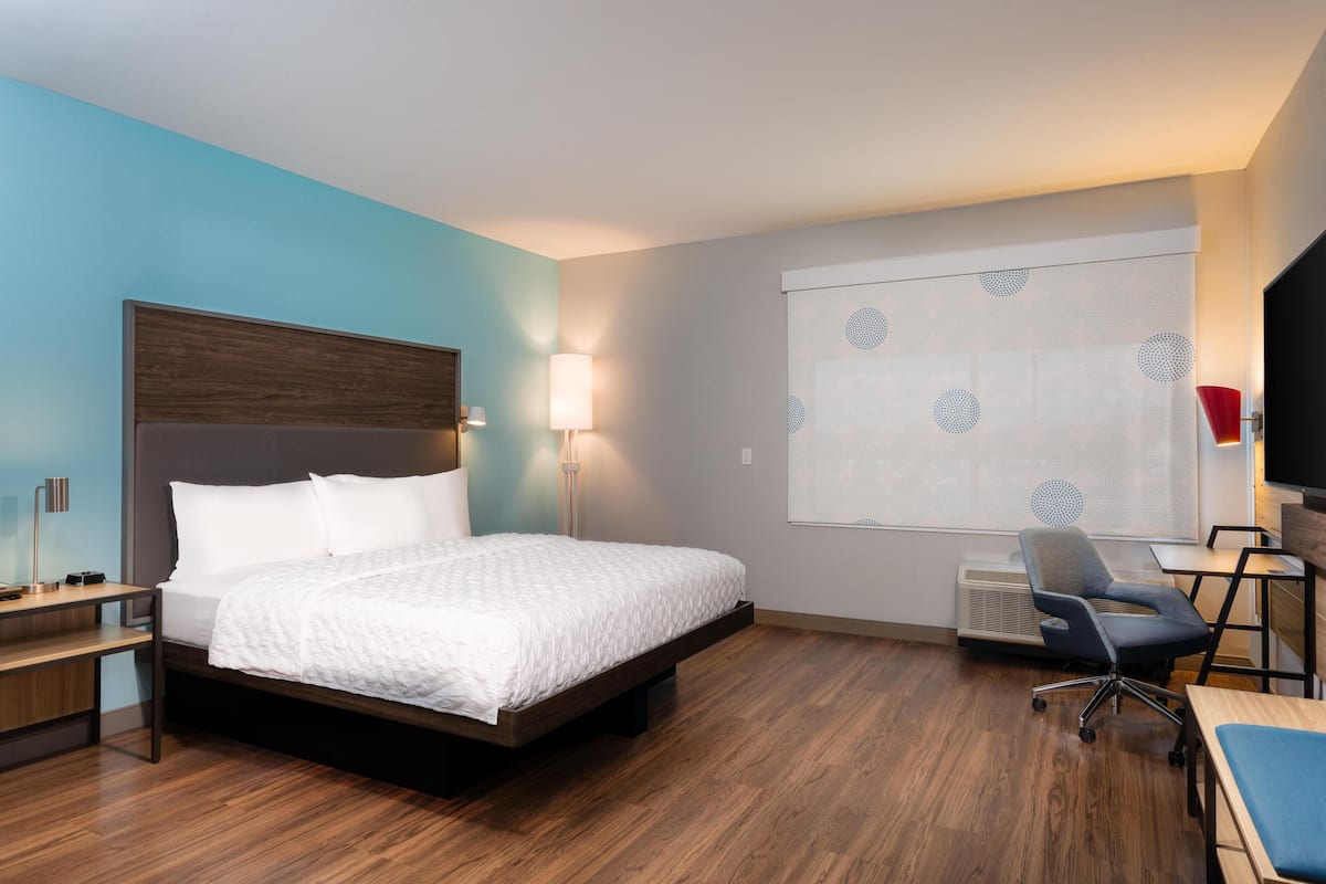 Quarto de hotel com cama, escrivaninha, cadeira e uma janela grande com vista.