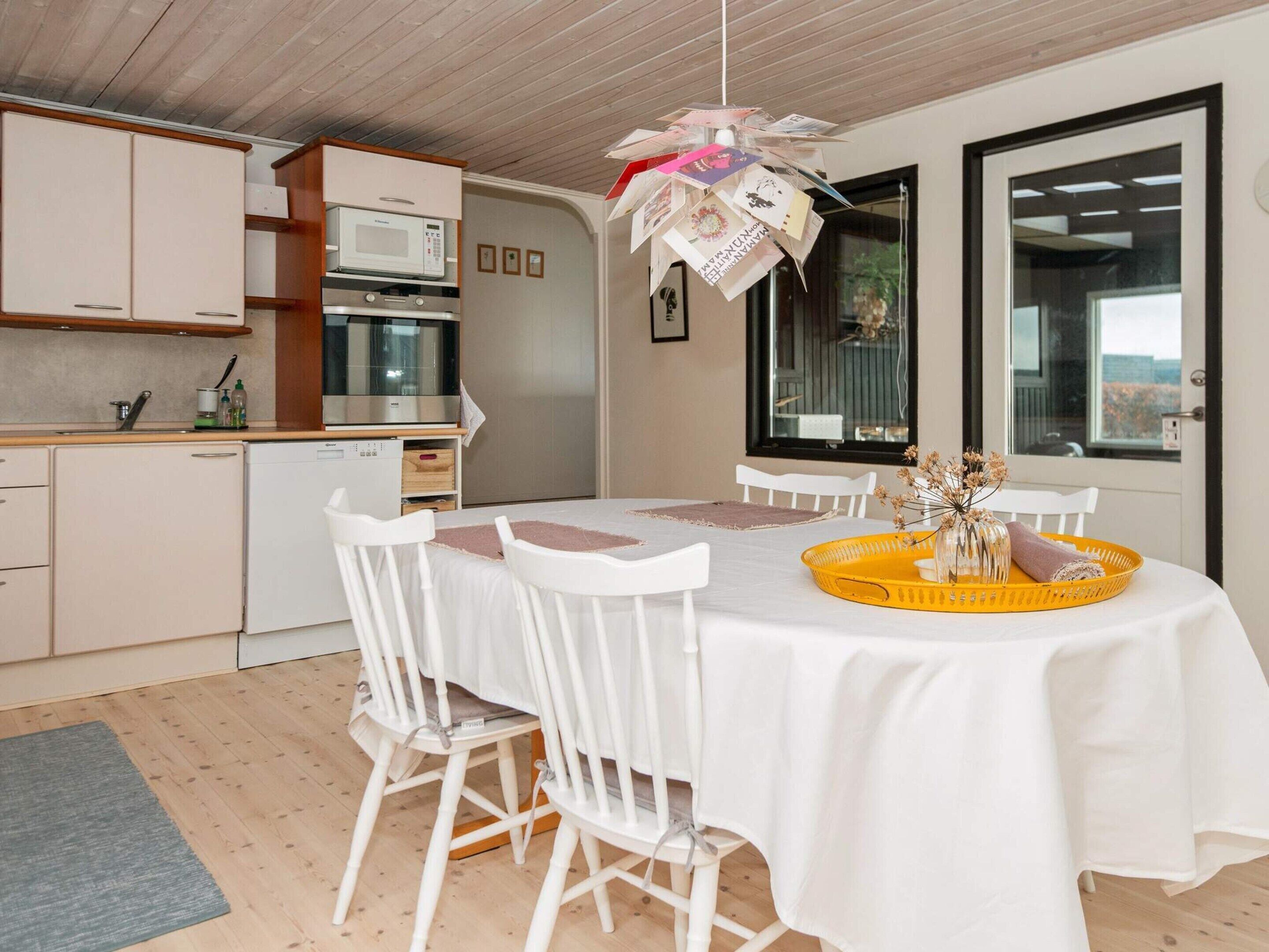 Uma cozinha moderna com armários brancos, uma mesa de jantar com cadeiras brancas e um tabuleiro amarelo com flores.