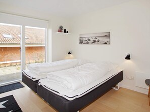 Quarto moderno com uma cama grande, vista para o exterior e uma pequena estante com objetos decorativos.
