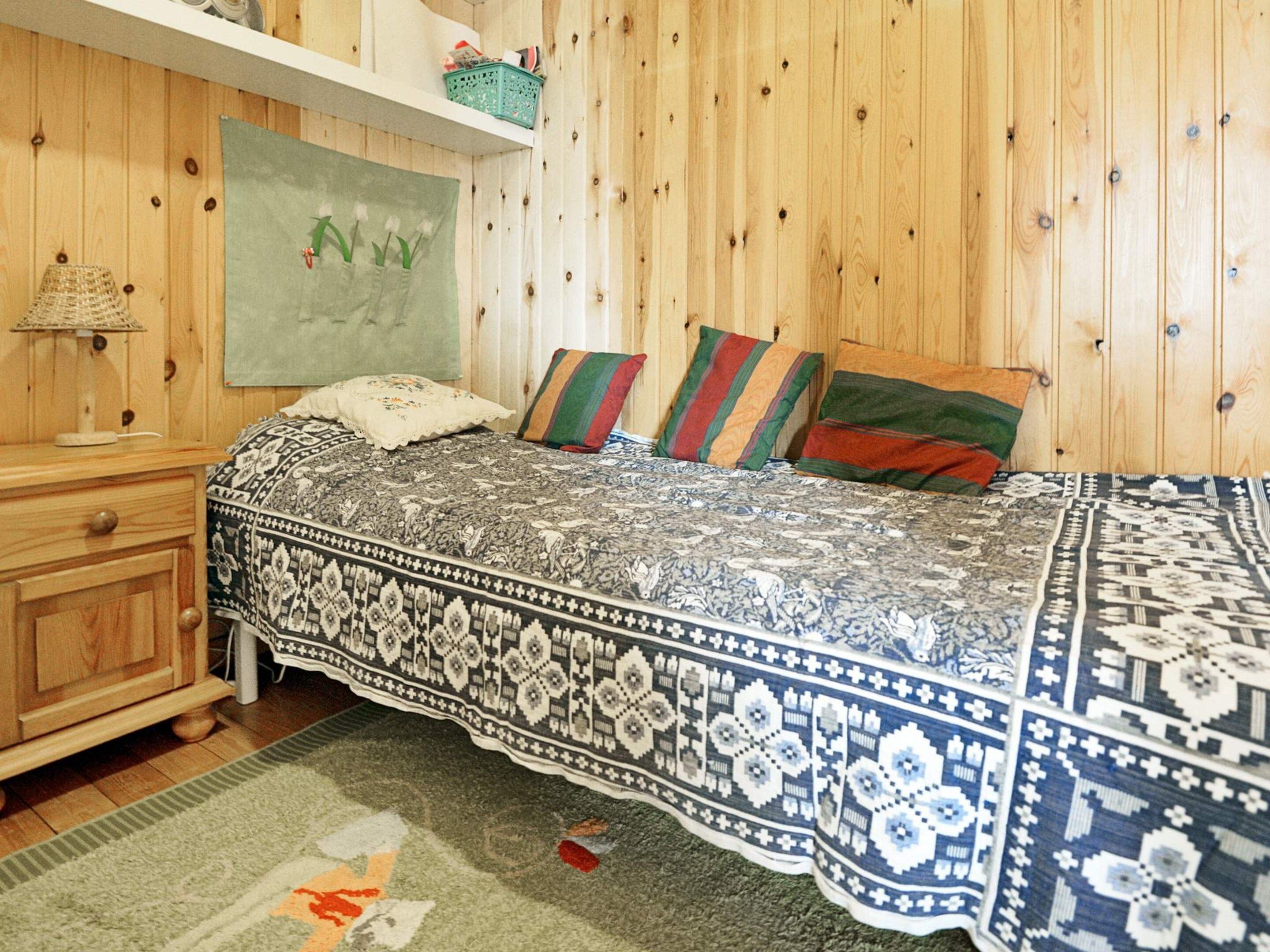 Quarto com painéis de madeira, uma cama, mesa de cabeceira, abajur e um quadro na parede.