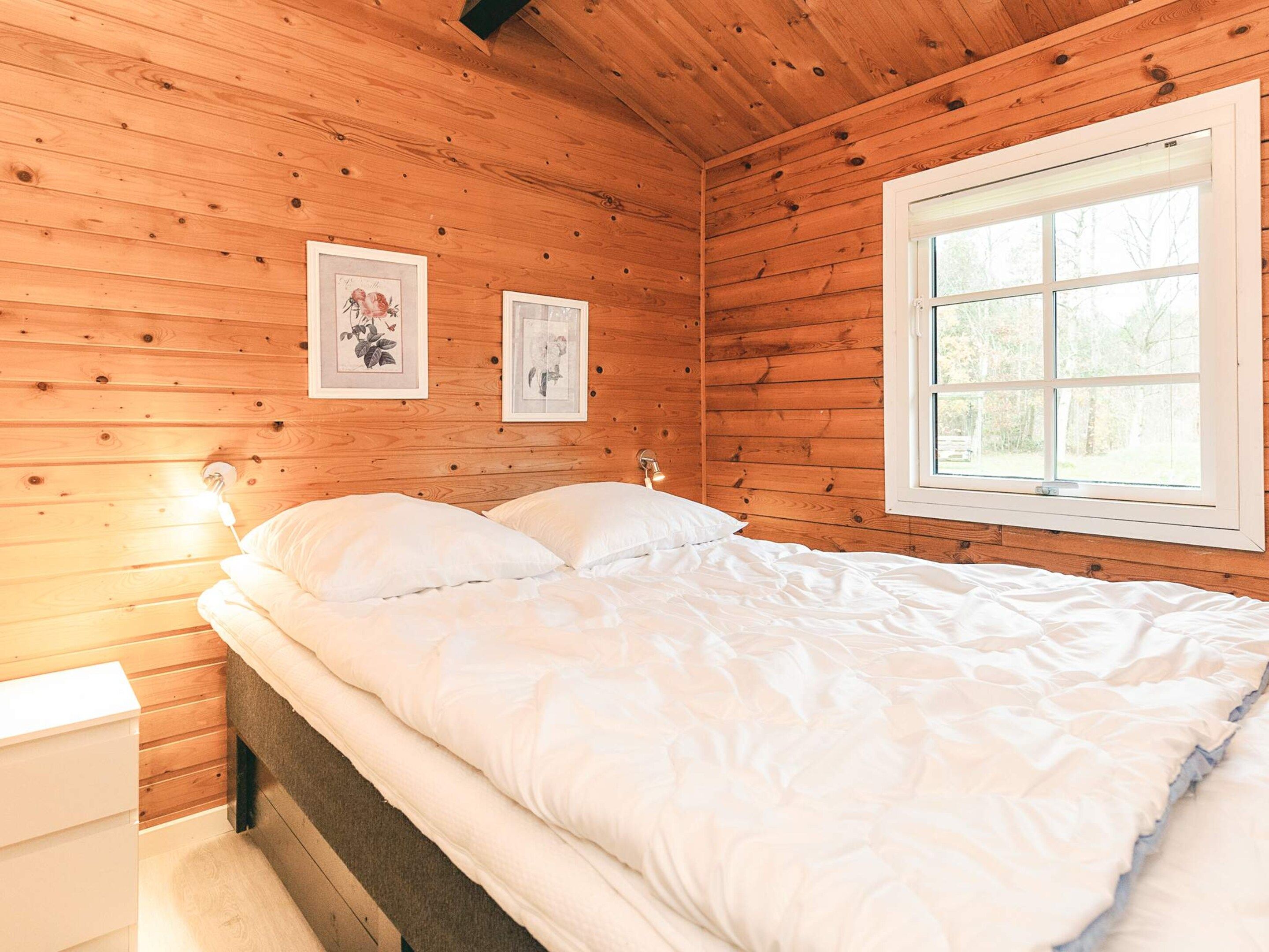 Quarto de cabana de madeira com uma cama, duas imagens emolduradas na parede e uma janela.