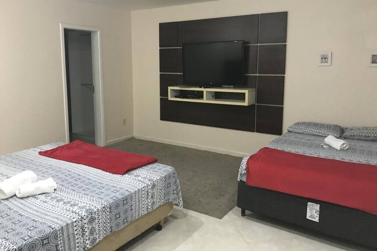 Quarto de hotel com duas camas, uma televisão fixada na parede e uma porta à esquerda.