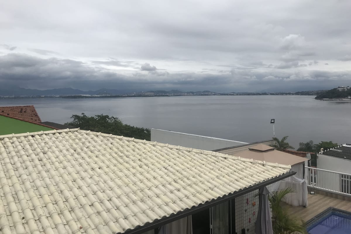 Vista de uma cidade costeira com um grande corpo de água, céu nublado e um edifício com telhado de azulejos.