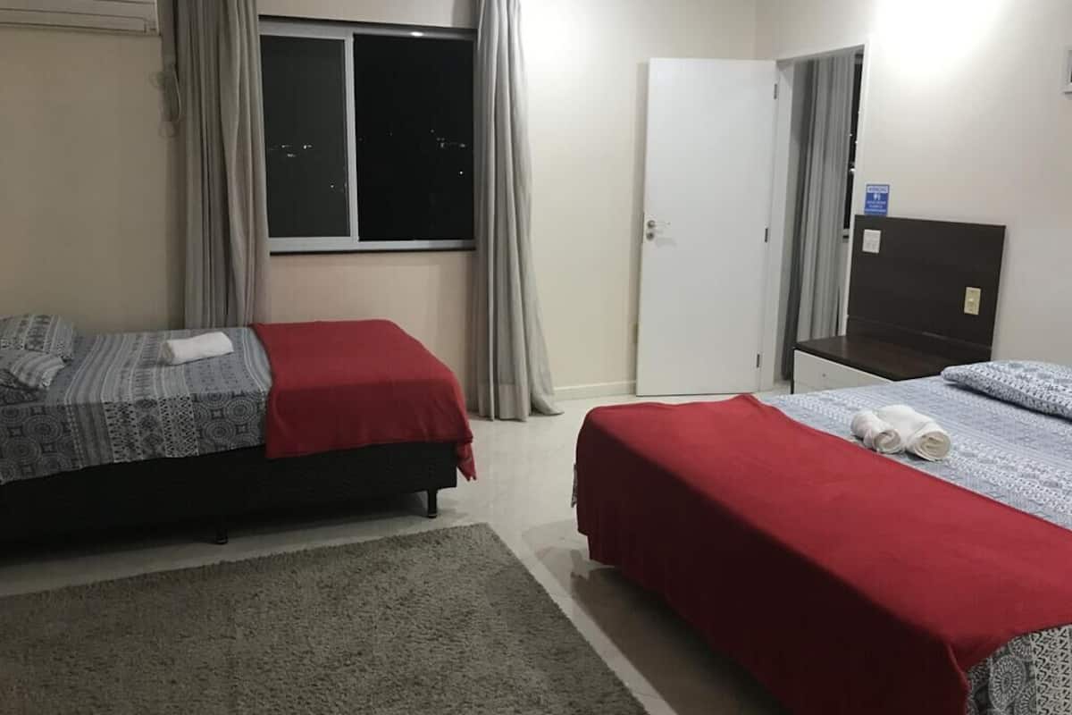 Quarto de hotel com duas camas, televisão, porta e janela.