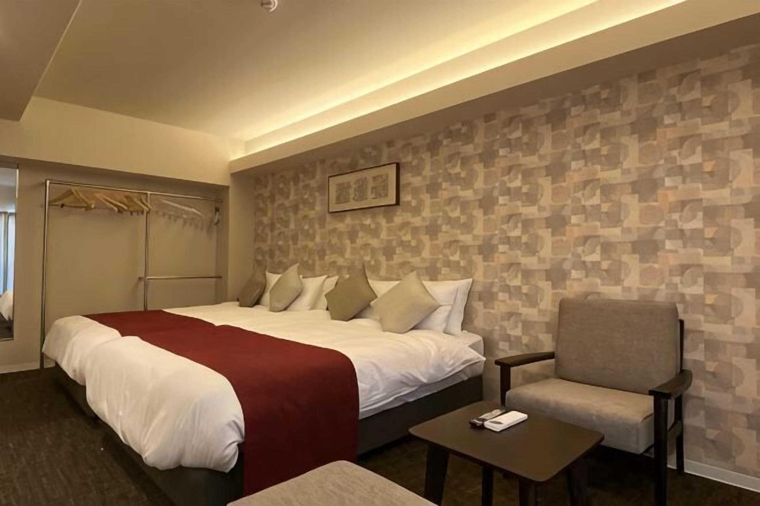 Quarto de hotel com cama, uma cadeira, uma mesa e um guarda-roupa.