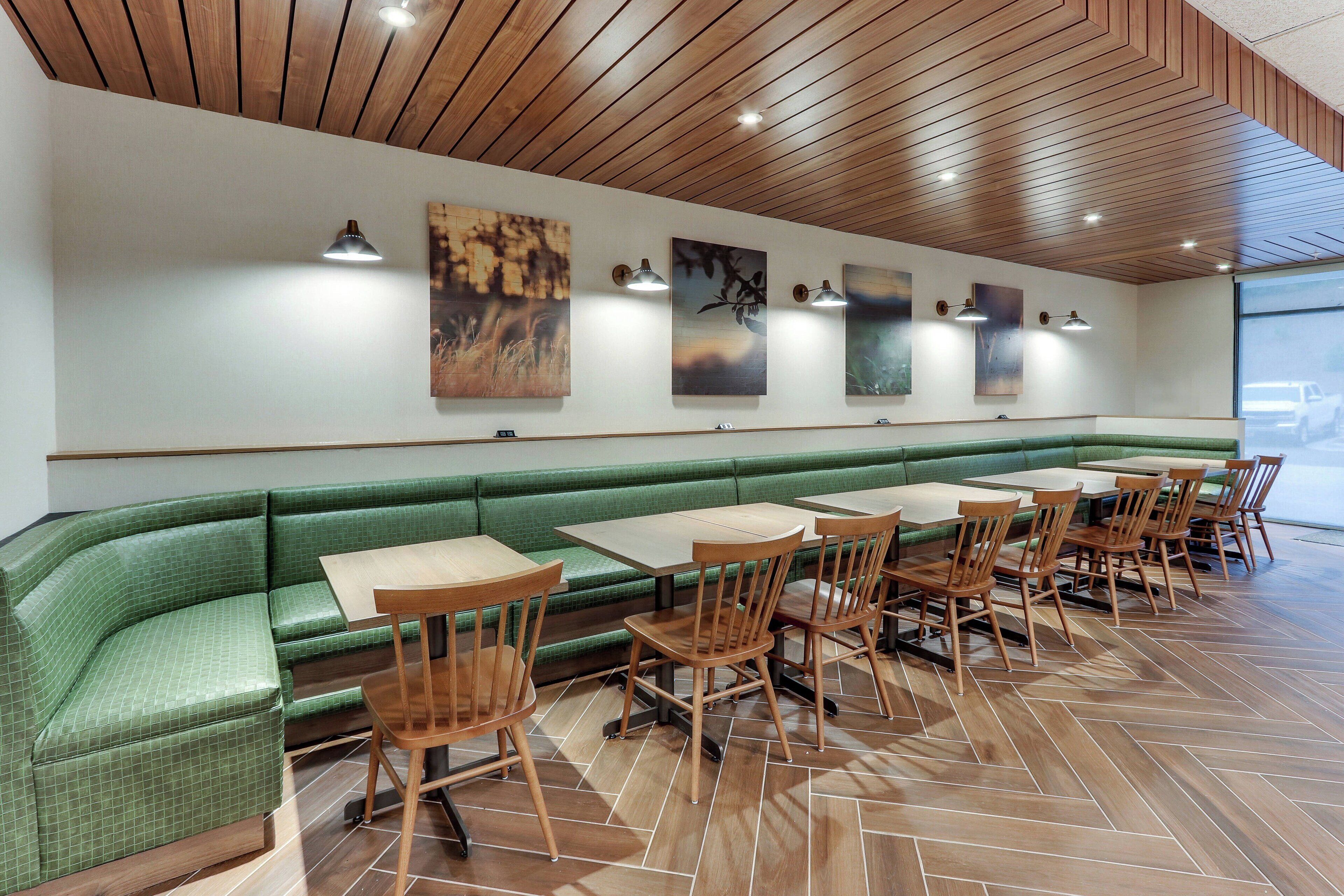 Um restaurante com área de estar em um banco acolchoado verde, mesas e cadeiras de madeira.