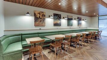 Um restaurante com área de estar em um banco acolchoado verde, mesas e cadeiras de madeira.