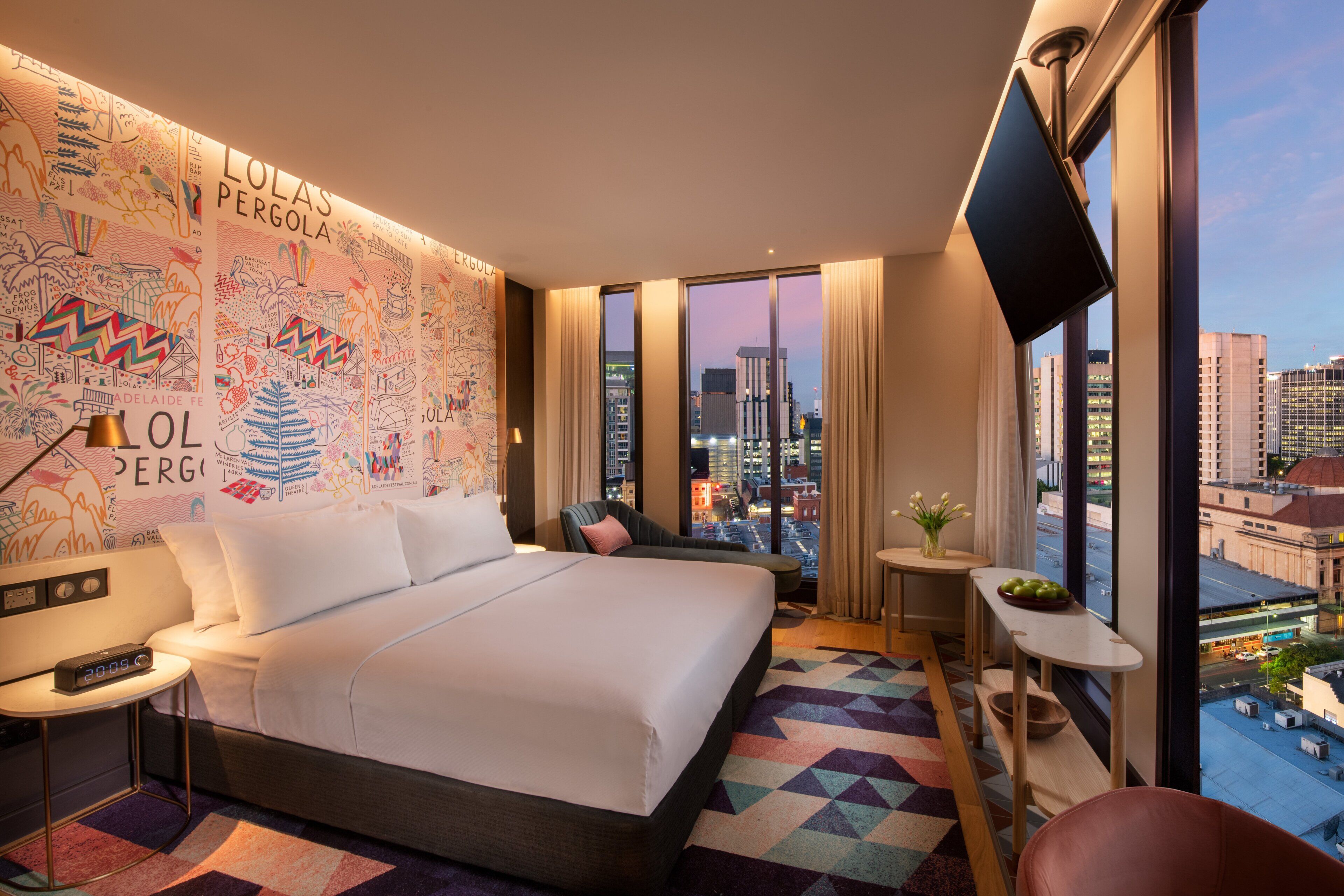 Quarto de hotel com uma cama grande, uma escrivaninha, uma cadeira, televisão e vista para a cidade.