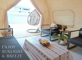 Um quarto em estilo tenda com uma cama, uma cadeira suspensa, um sofá e uma pequena mesa com uma planta.