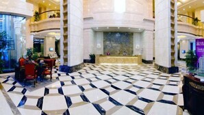 Um hall com piso xadrez, colunas de mármore e uma mesa de recepção.