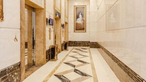 Corredor com piso de mármore, um grande retrato na parede e sinalização de acessibilidade para cadeiras de rodas.