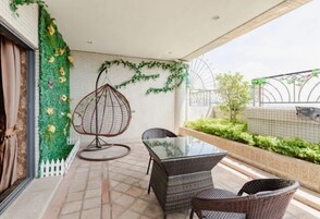 Uma varanda com móveis de vime, uma cadeira suspensa e uma mesa com tampo de vidro.