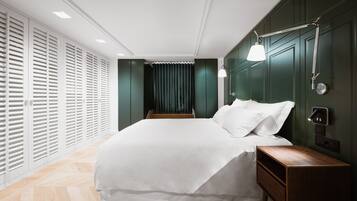 Quarto moderno com cama grande, mesa de cabeceira de madeira e luminária fixada na parede.