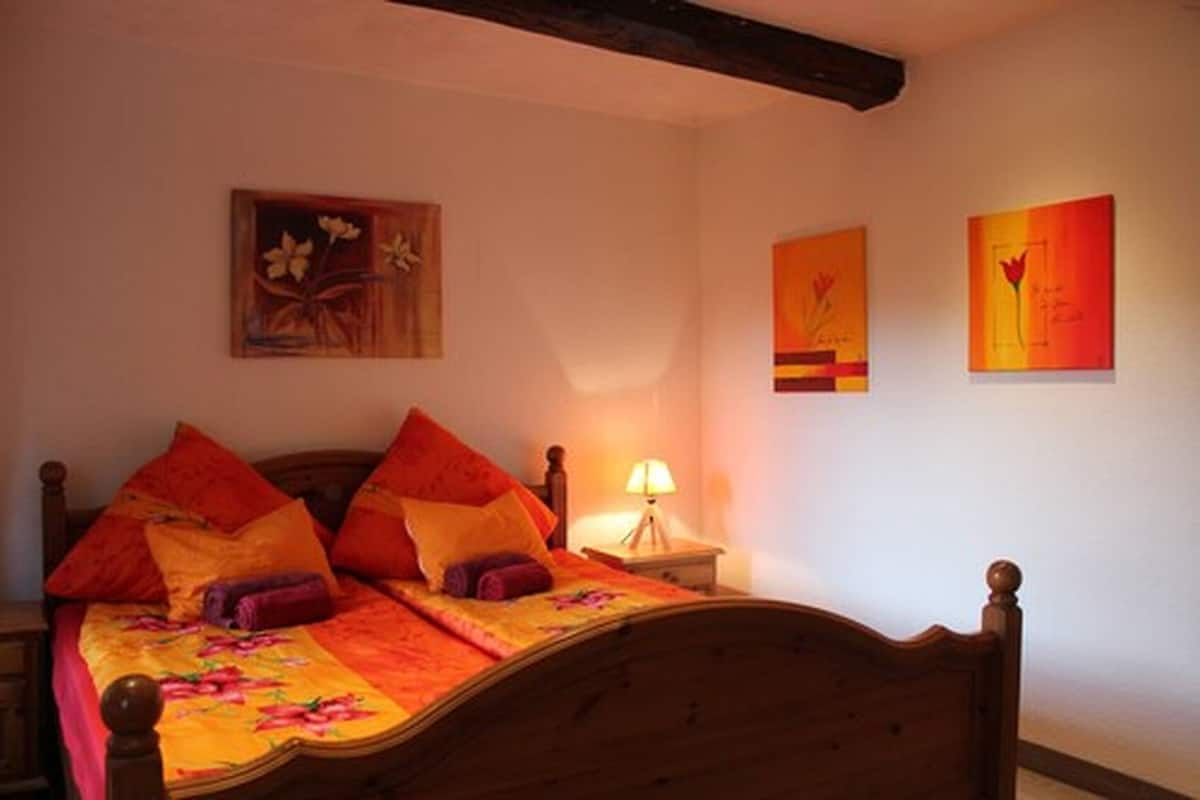 Quarto com cama de madeira, roupa de cama colorida e quadros nas paredes.