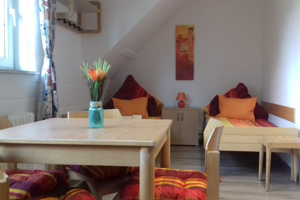 Um quarto acolhedor com uma mesa de madeira, duas cadeiras, um sofá e uma pequena mesa com uma luminária.