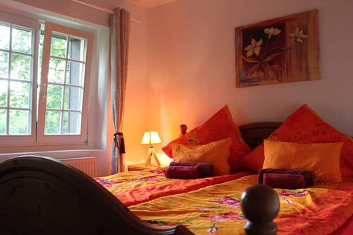 Um quarto com uma cama, janela, luminária e um quadro na parede.