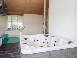 Um espaço de spa com hidromassagem, janela com vista e teto de madeira.