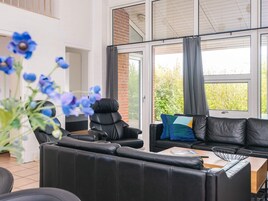 Uma sala de estar moderna com um sofá e uma poltrona de couro preto, e uma mesa de centro de madeira. Há uma janela grande com vista para o verde lá fora.