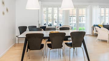 Uma sala de jantar moderna com uma mesa comprida e cadeiras, janelas amplas e um pendente.