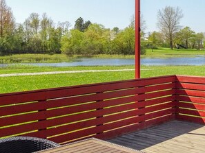 Um deck de madeira com um banco vermelho, com vista para um lago e árvores.
