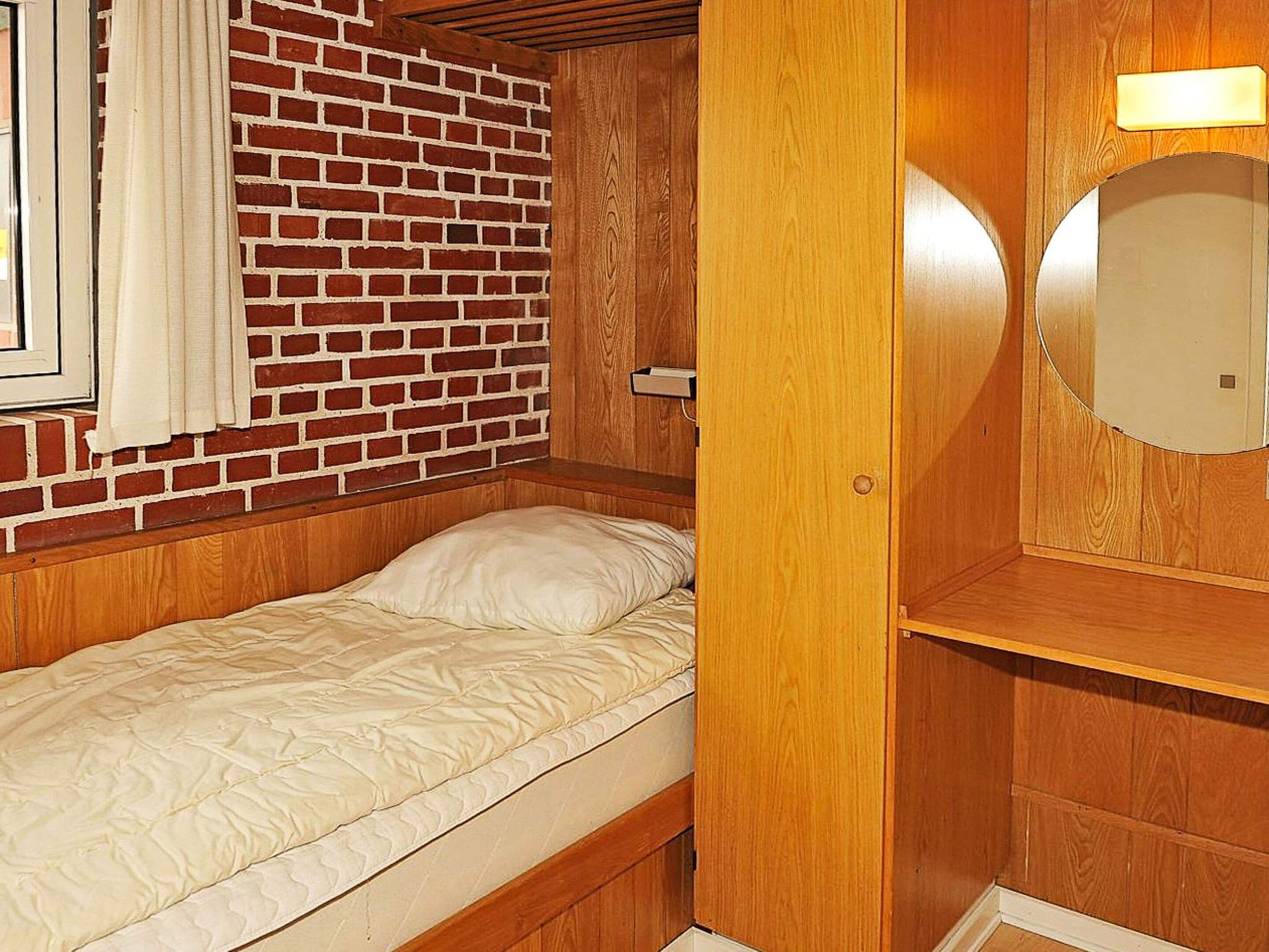 Uma cama de solteiro com cabeceira de madeira, parede de tijolos e espelho com moldura redonda.
