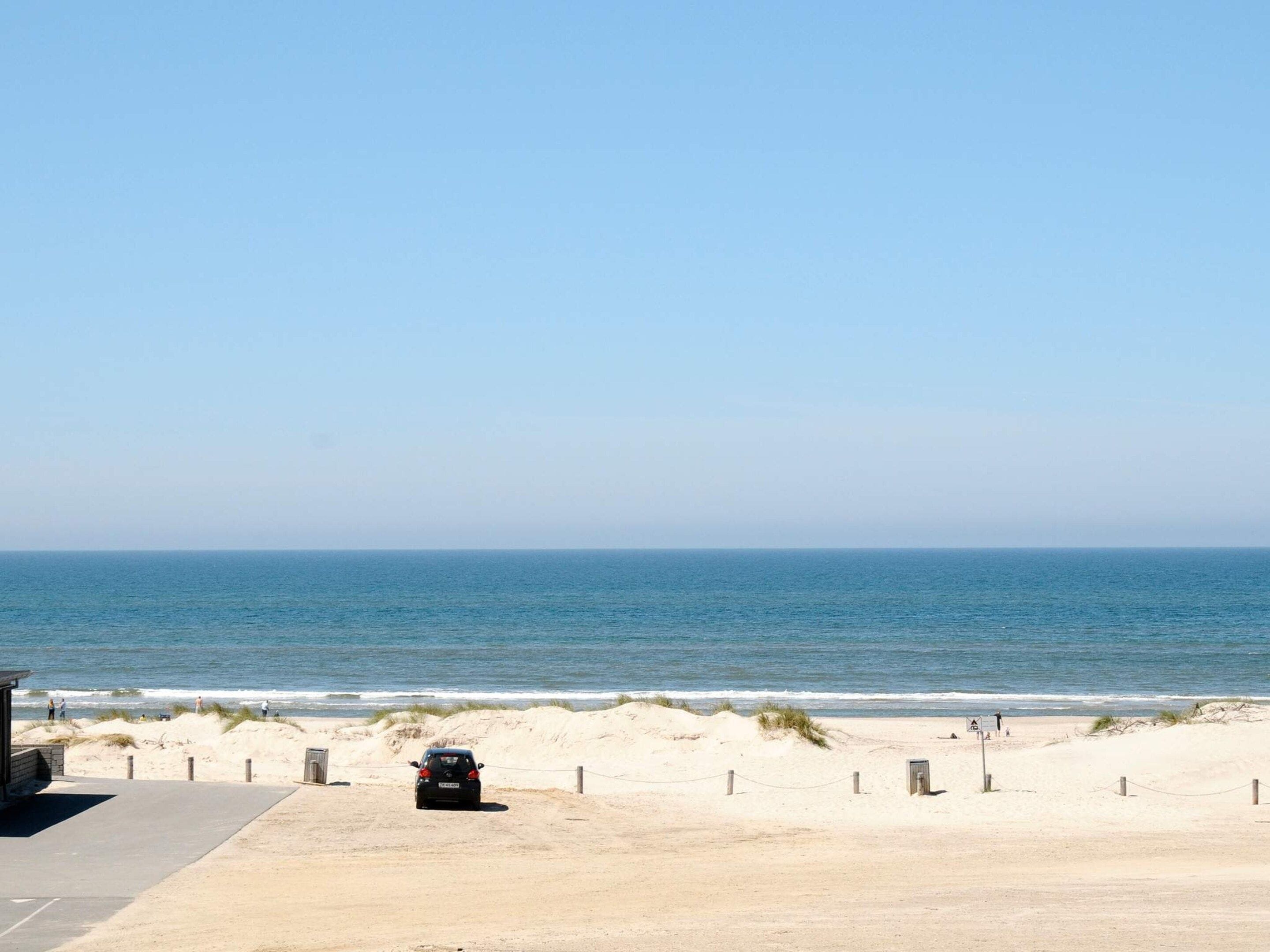 Praia com área de estacionamento e um edifício ao primeiro plano.