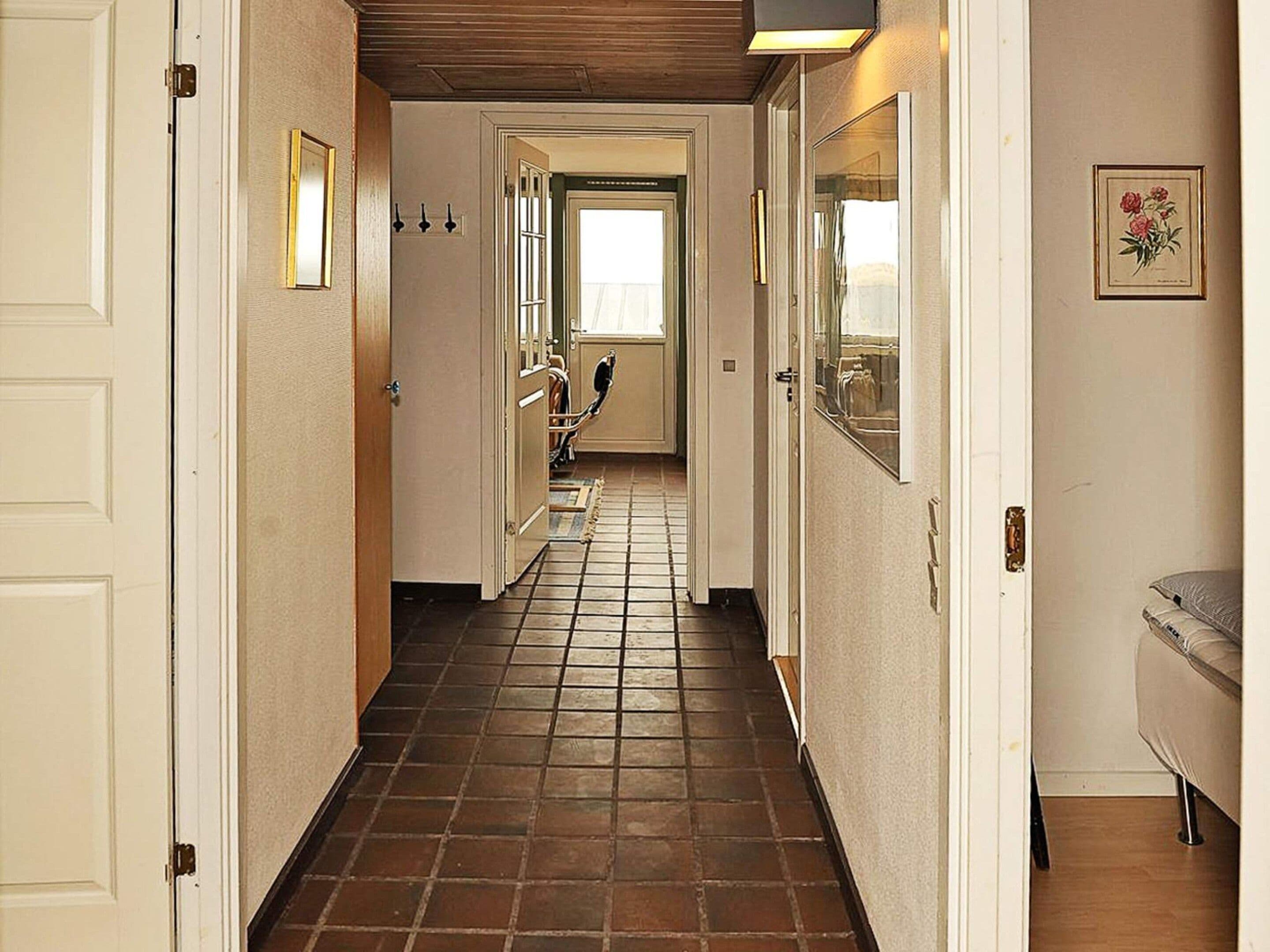 Um corredor com piso de azulejos, paredes brancas e uma porta no final.