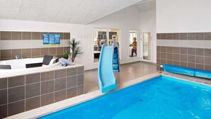 Piscina interna com escorregador, área de recepção com placa informativa azul e uma pessoa ao fundo.