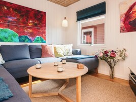 Uma sala de estar moderna com um sofá seccional, uma mesa de centro redonda de madeira e um grande quadro abstrato.