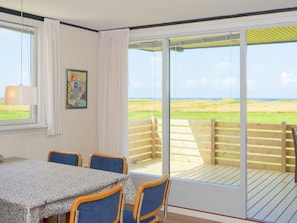 Quarto com mesa e cadeiras, um quadro na parede e vista para o exterior por uma porta deslizante.