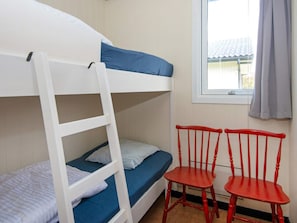 Uma cama beliche com escada, duas cadeiras vermelhas e janela com vista para um prédio.
