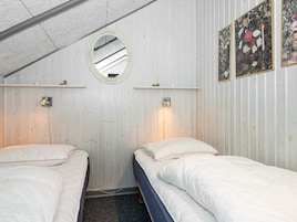 Quarto com duas camas, um espelho redondo e luminárias fixadas na parede.