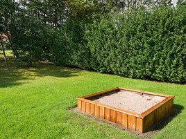 Um canteiro elevado com base de cascalho, rodeado por um gramado e uma sebe densa.