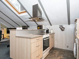 Cozinha compacta com fogão, forno e micro-ondas embutidos, bancada de madeira e claraboia.