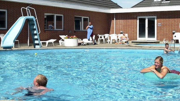 Uma piscina com escorregador, espreguiçadeiras e um edifício de tijolos ao fundo.